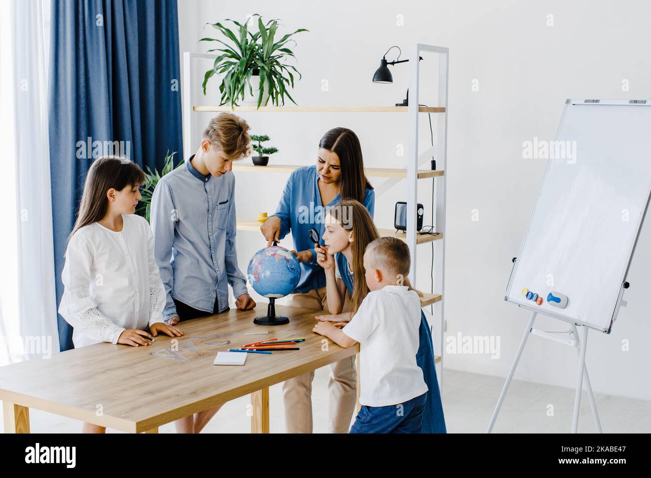 Teacher and children in class are looking at globe, teacher helps ...
