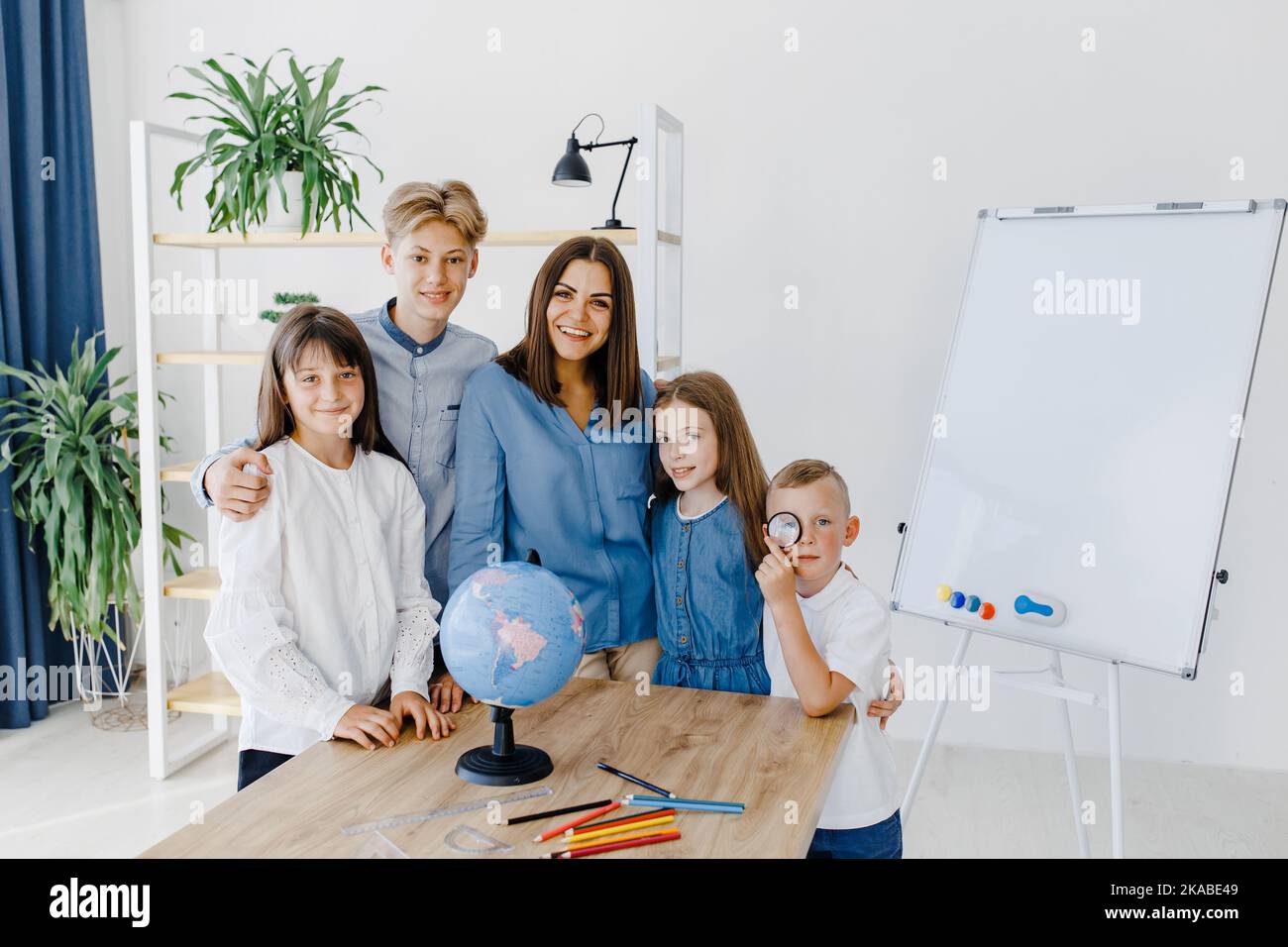 Teacher and children in class are looking at globe, teacher helps ...
