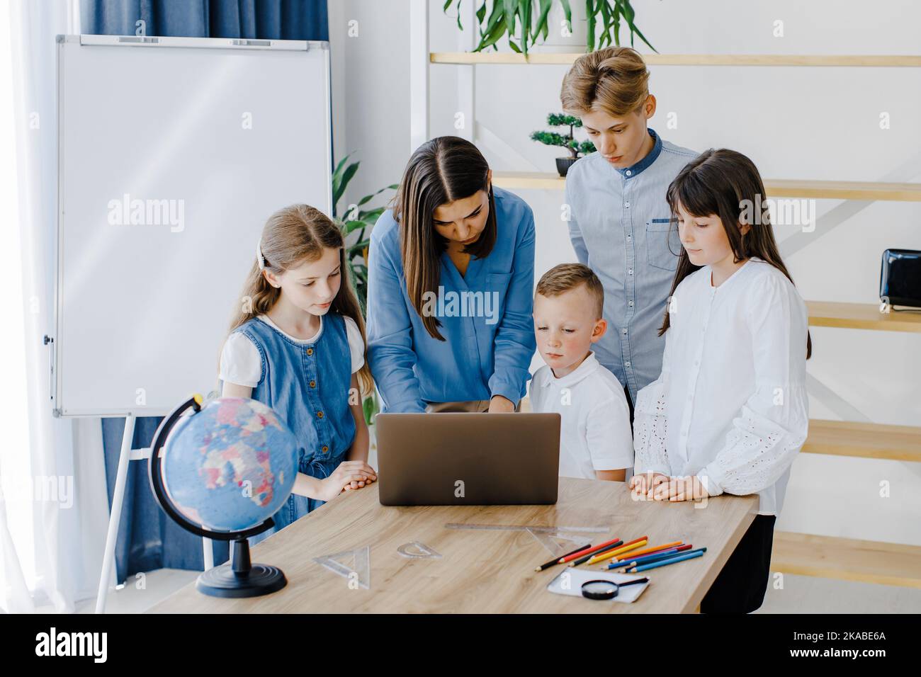 Happy diverse junior school children students gathered at teacher table ...