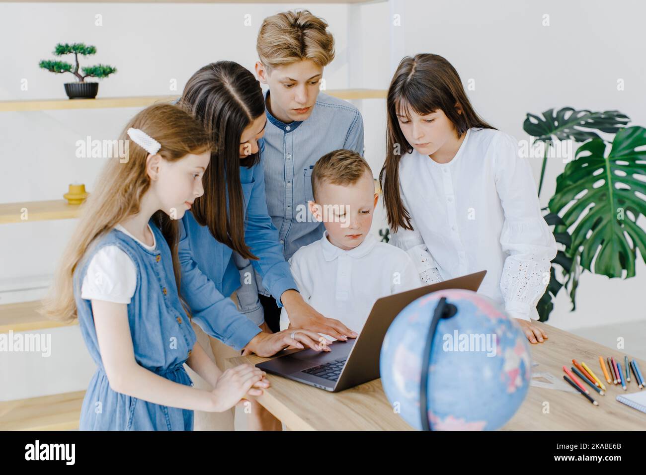 Happy diverse junior school children students gathered at teacher table ...