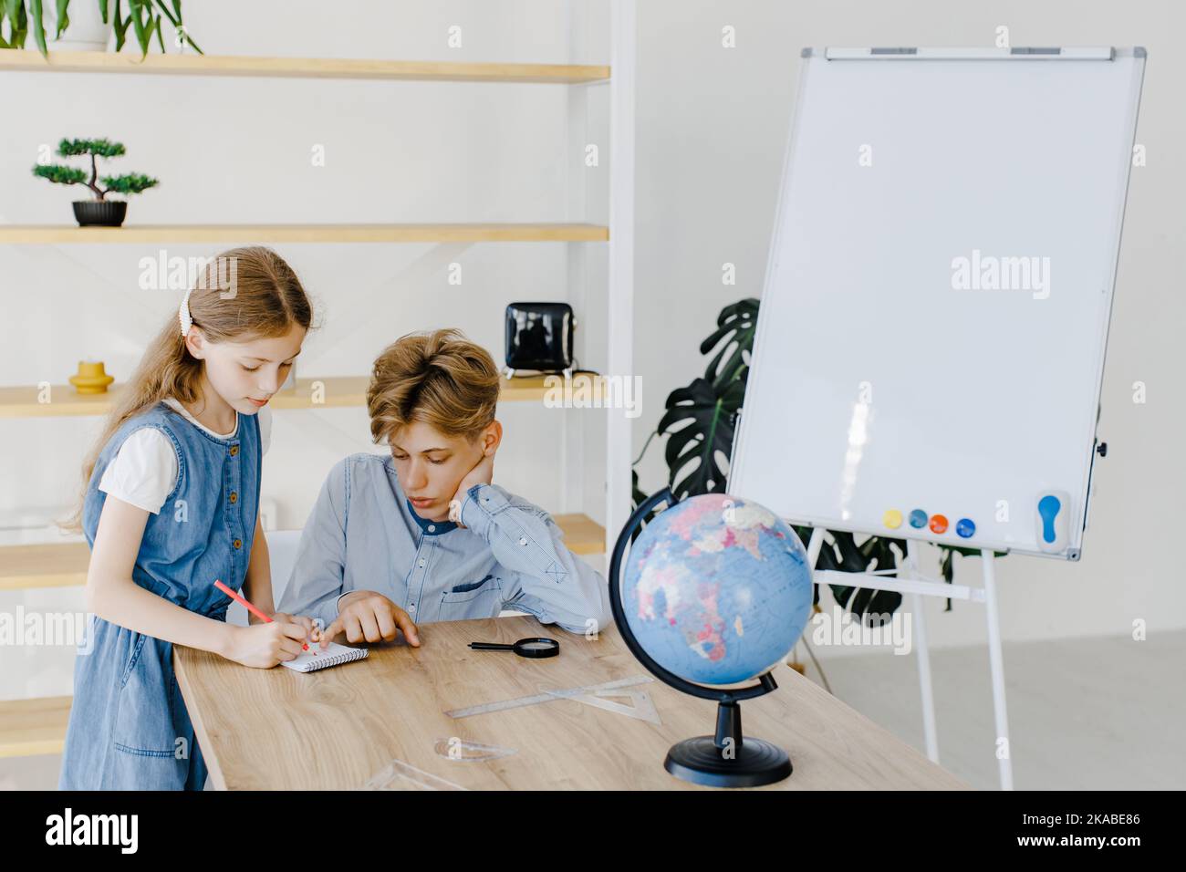 Teenage girl and boy siting near table with globe in classroom. Teen ...