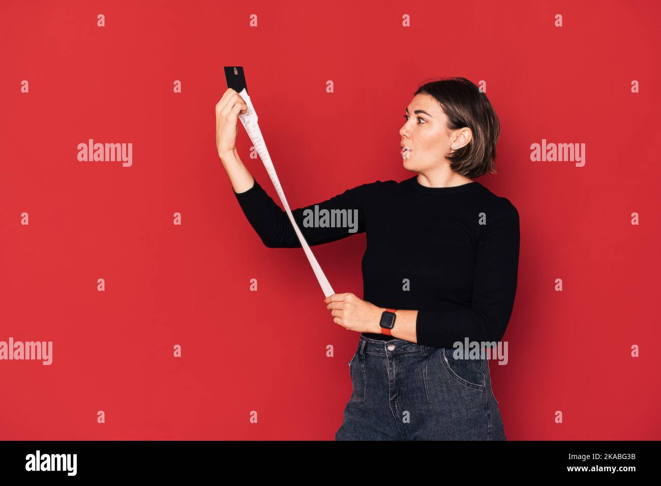 Lady looking at long shopping receipt holding credit card against red ...