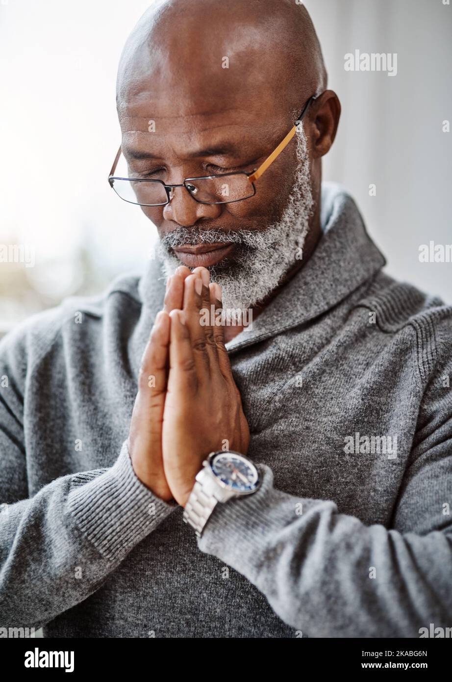 Prayer helps him keep going. a handsome senior man praying in his home ...