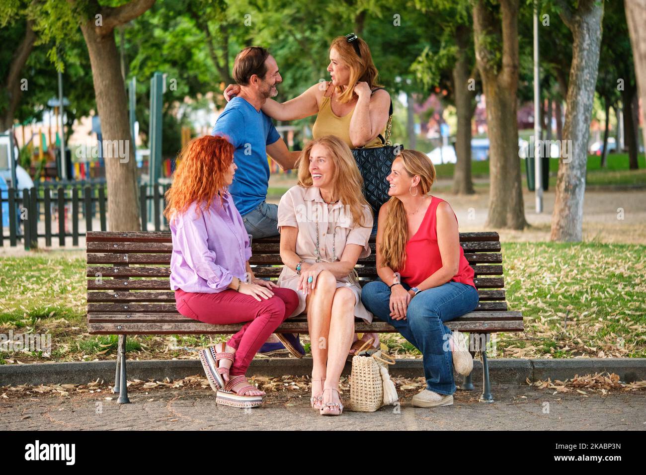 Five mature adults talking and laughing sitting on a bench in a park ...