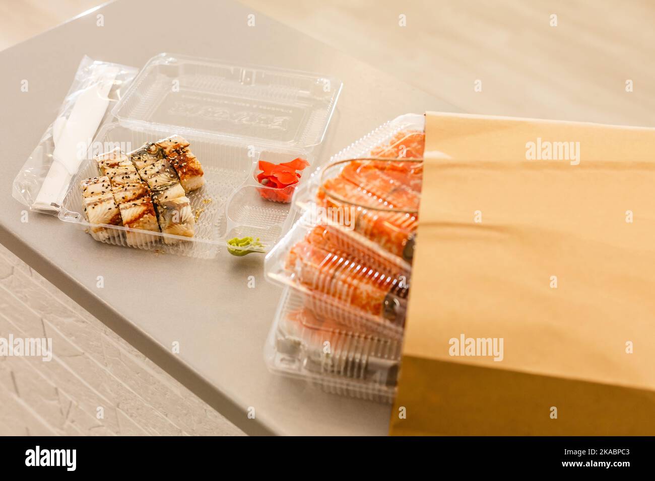Sushi rolls in plastic box near paper package on white table. Delivery ...