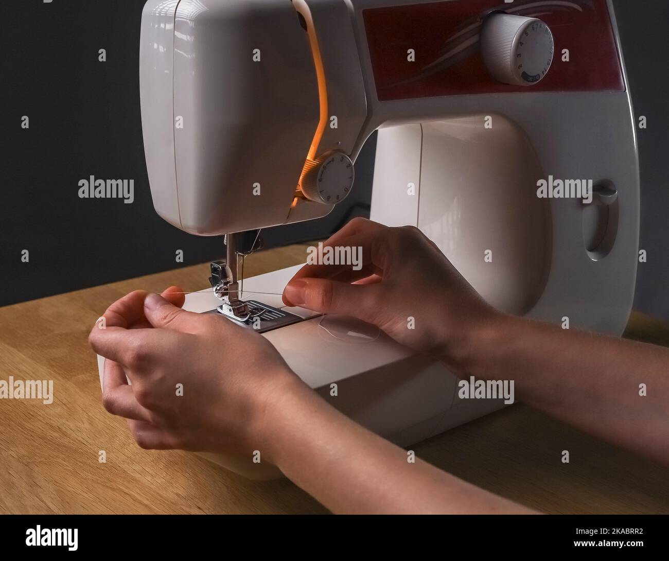 Seamstress hands inserting thread through needle hole in sewing machine ...
