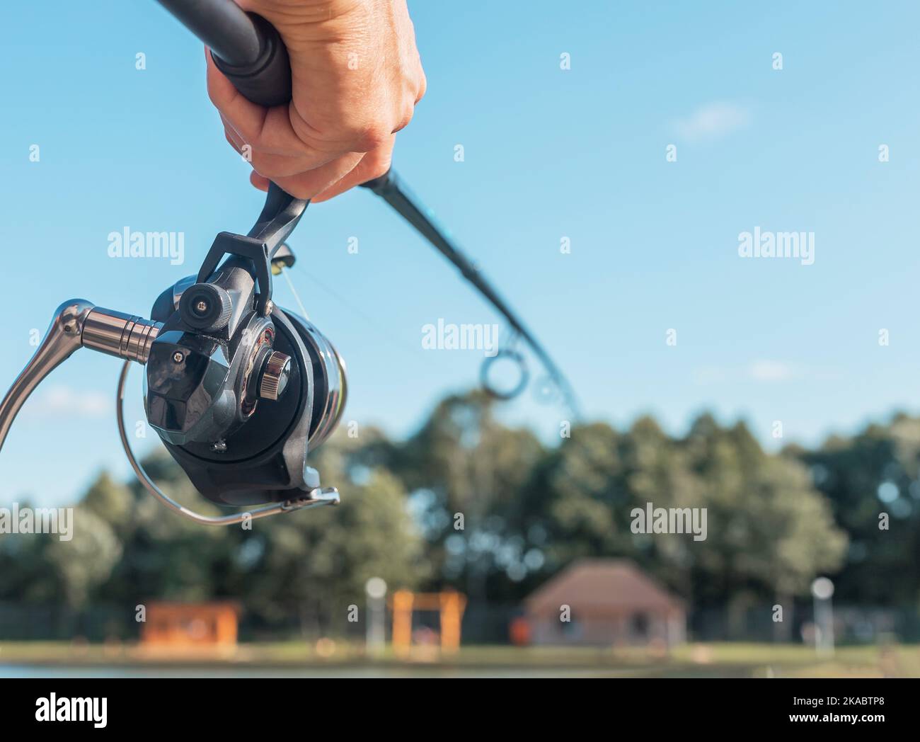 Hand closeup holding fishing rod over blue clear sky on summer holidays ...