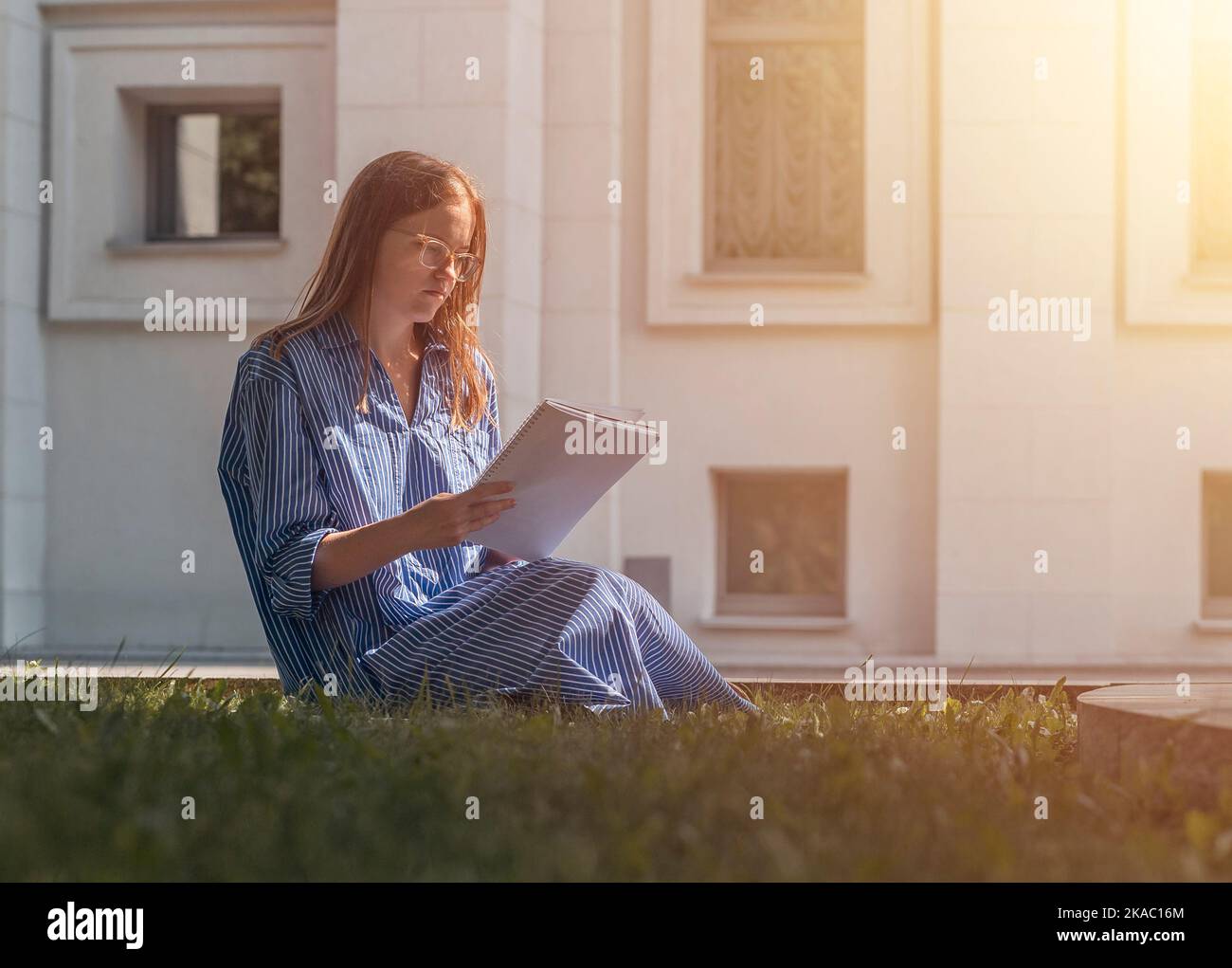 Young woman student sitting on grass near university building and ...
