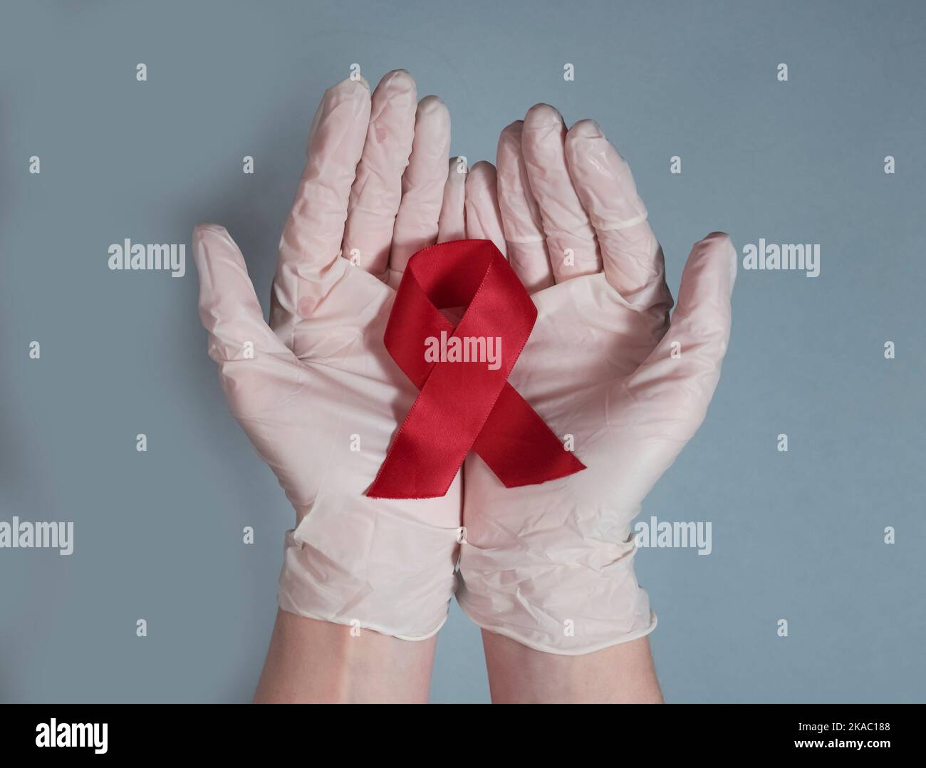 Red ribbon bow for AIDS and HIV awareness, in doctor hand close up ...
