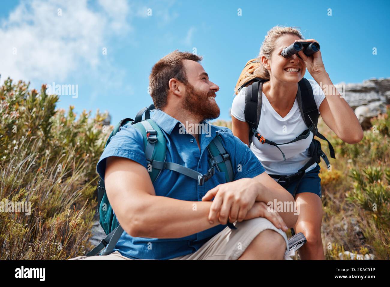 Woman hiking, using binoculars and couple adventure happy together with smile in nature on ...
