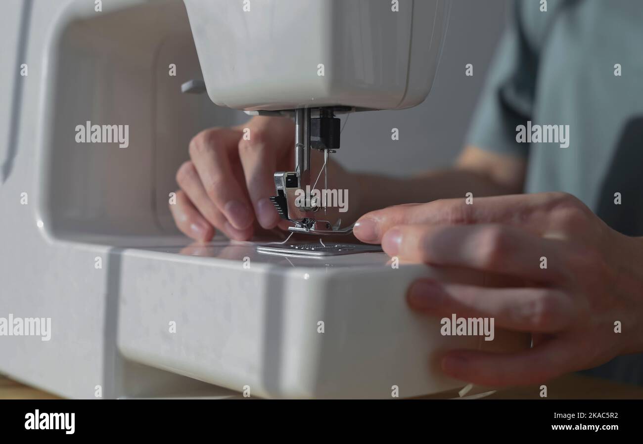 Female hands inserting thread through needle hole in sewing machine ...