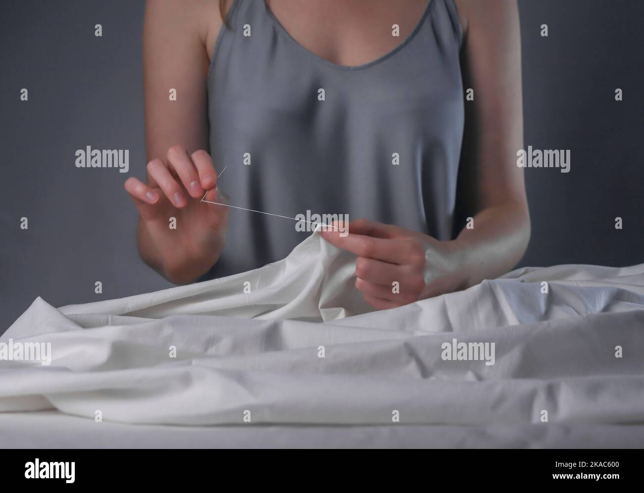 Hands inserting thread through needle hole for sewing at her wood desk ...