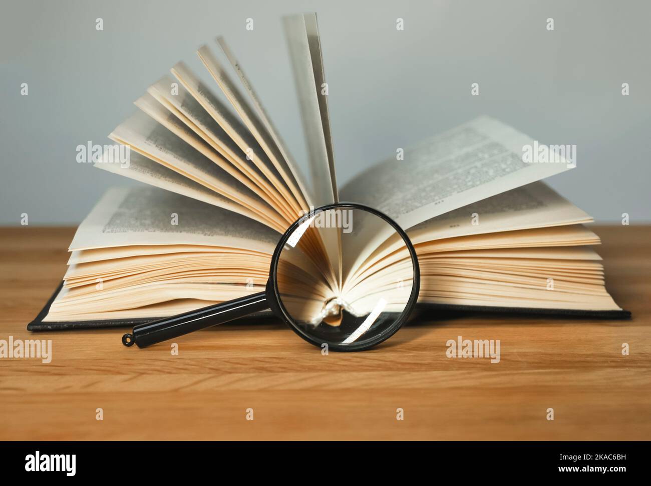 Magnifying glass and open books with turning pages on wood table ...