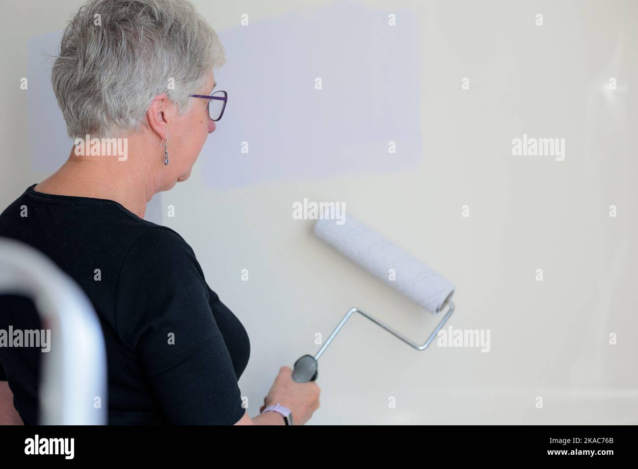 Mature woman starting to use paint roller on a wall Stock Photo - Alamy