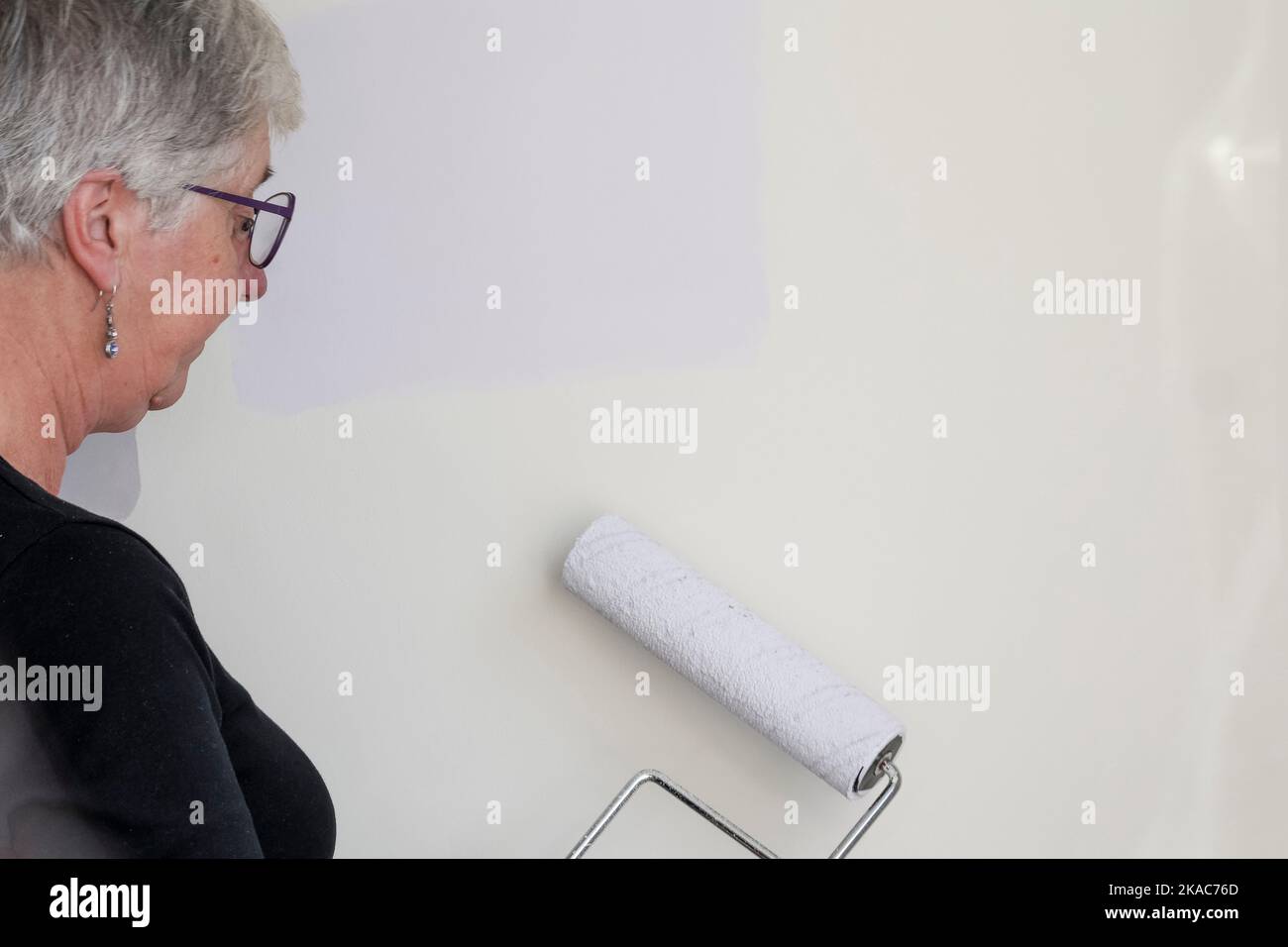 Mature woman starting to use paint roller on a wall Stock Photo - Alamy