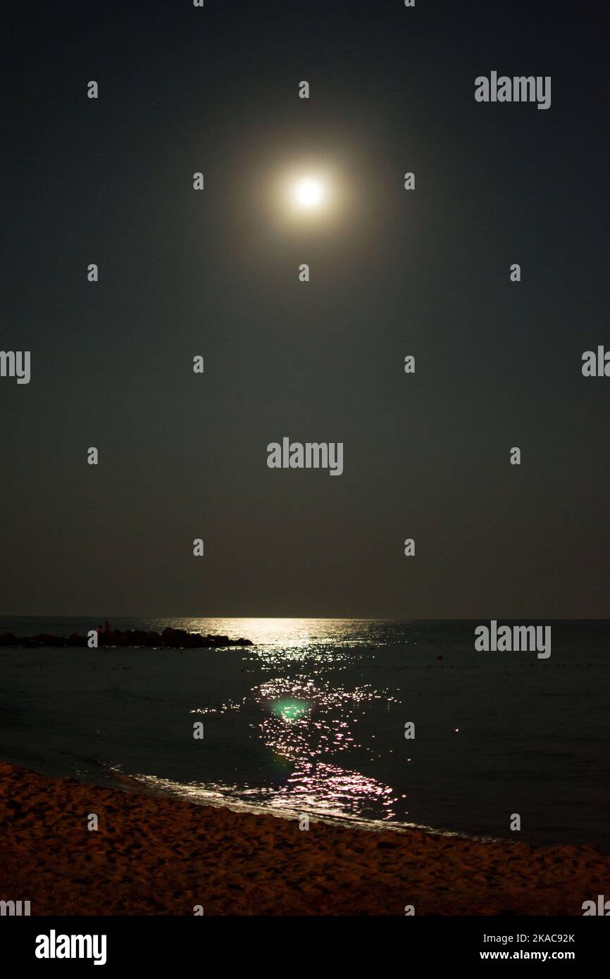 Lunar path on black night on calm water among the rocks. Vertical photo ...