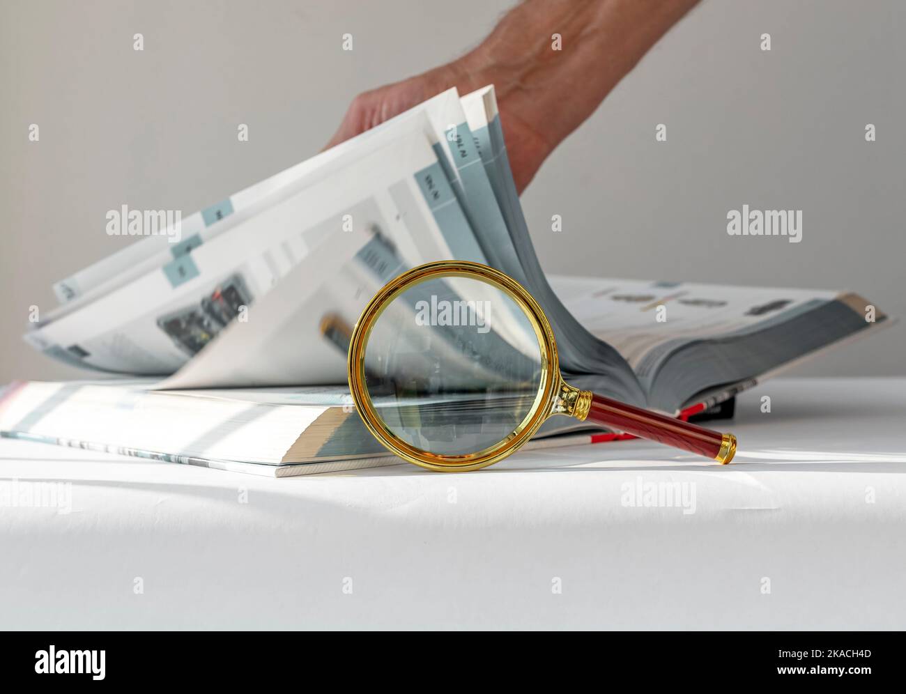 Technical book with turning pages, male hand and magnifying glass ...