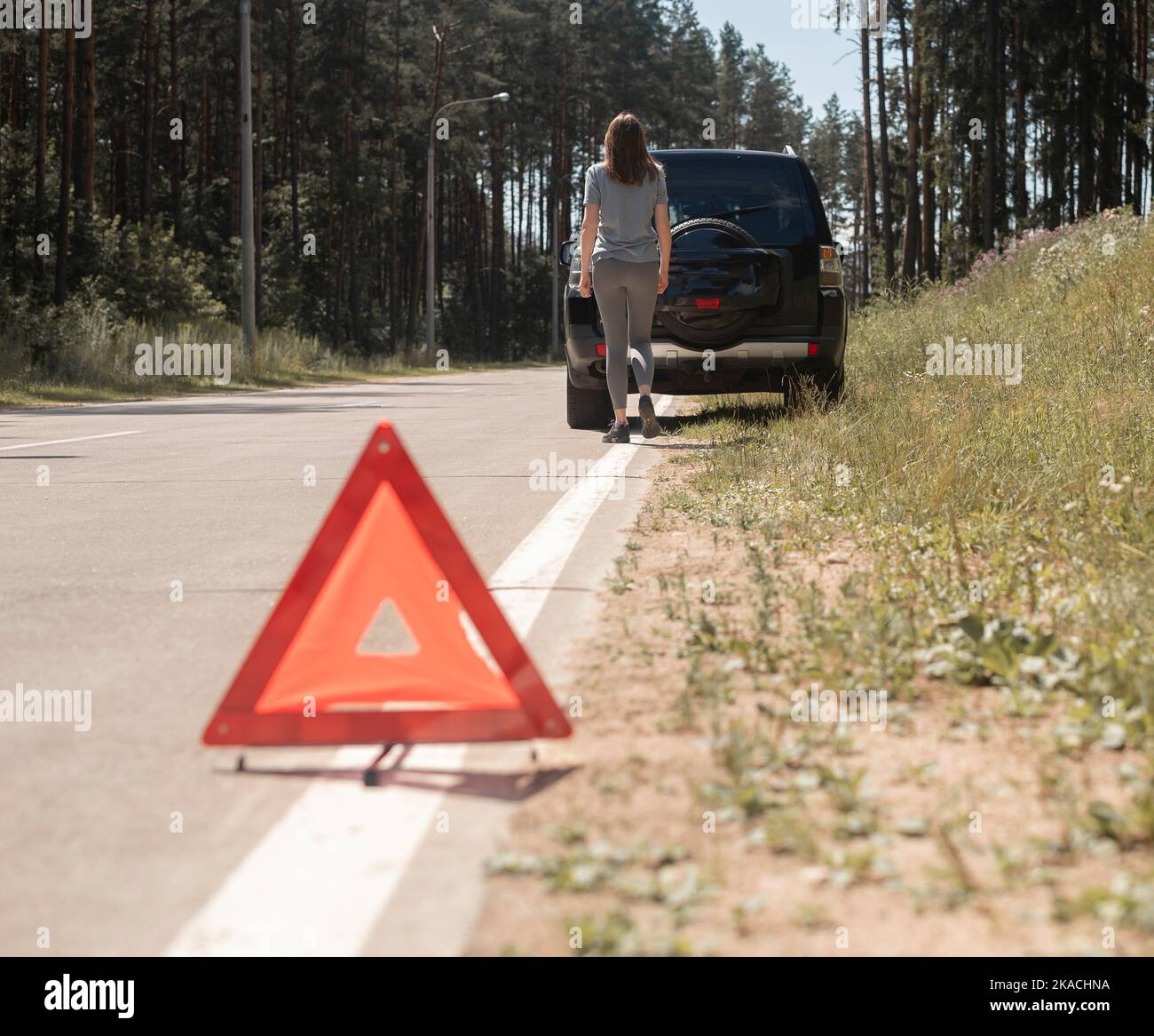 Triangle caution sign closeup on road with young woman going to car on ...