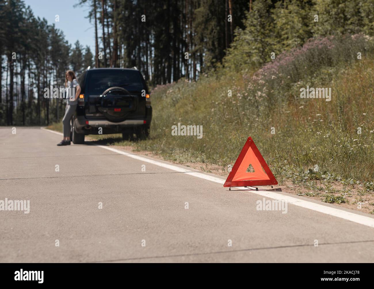 Triangle caution sign on roadside after car breakdown and woman driver ...