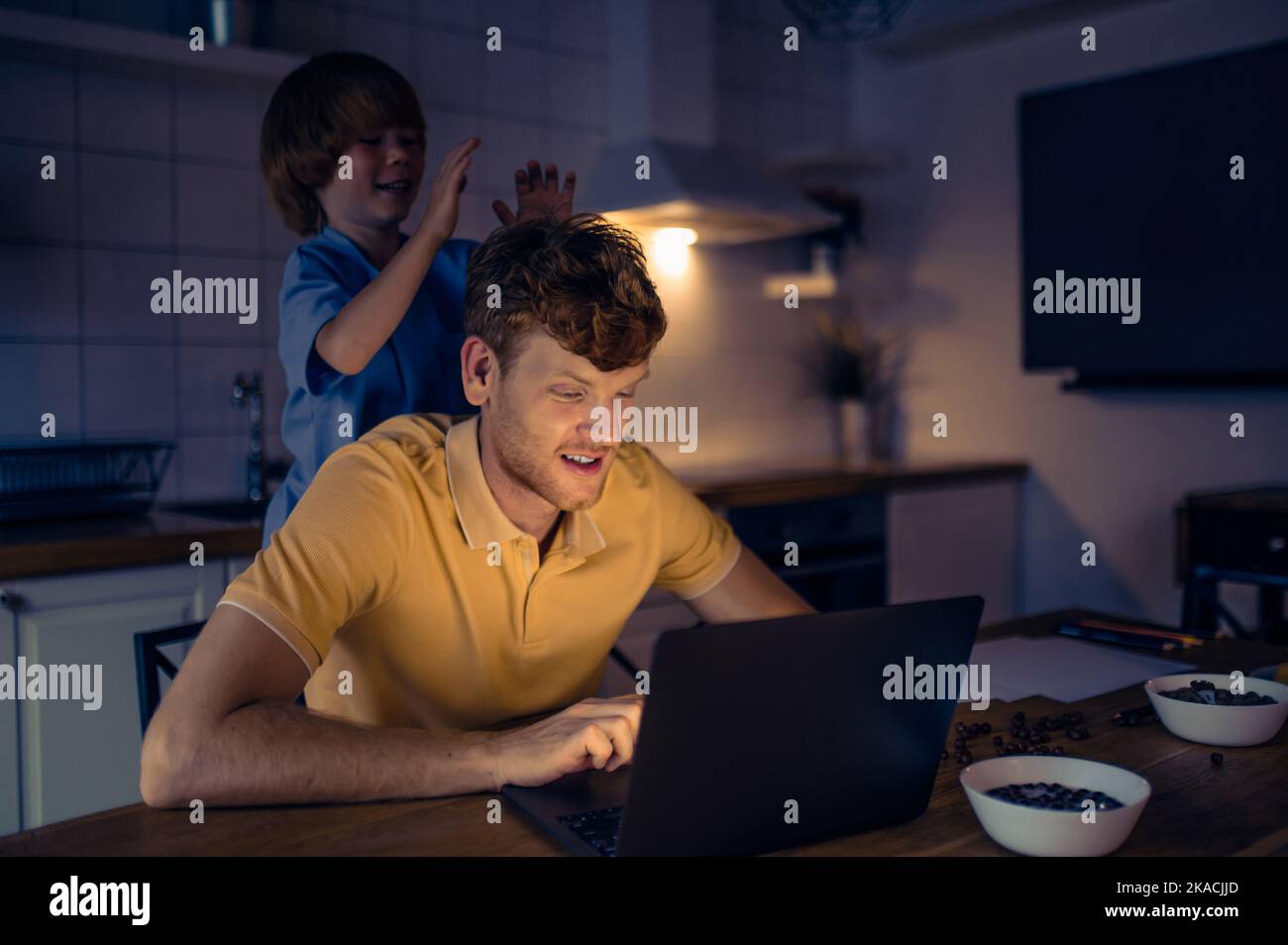 Dad working on a laptop while his son playing next to him Stock Photo ...