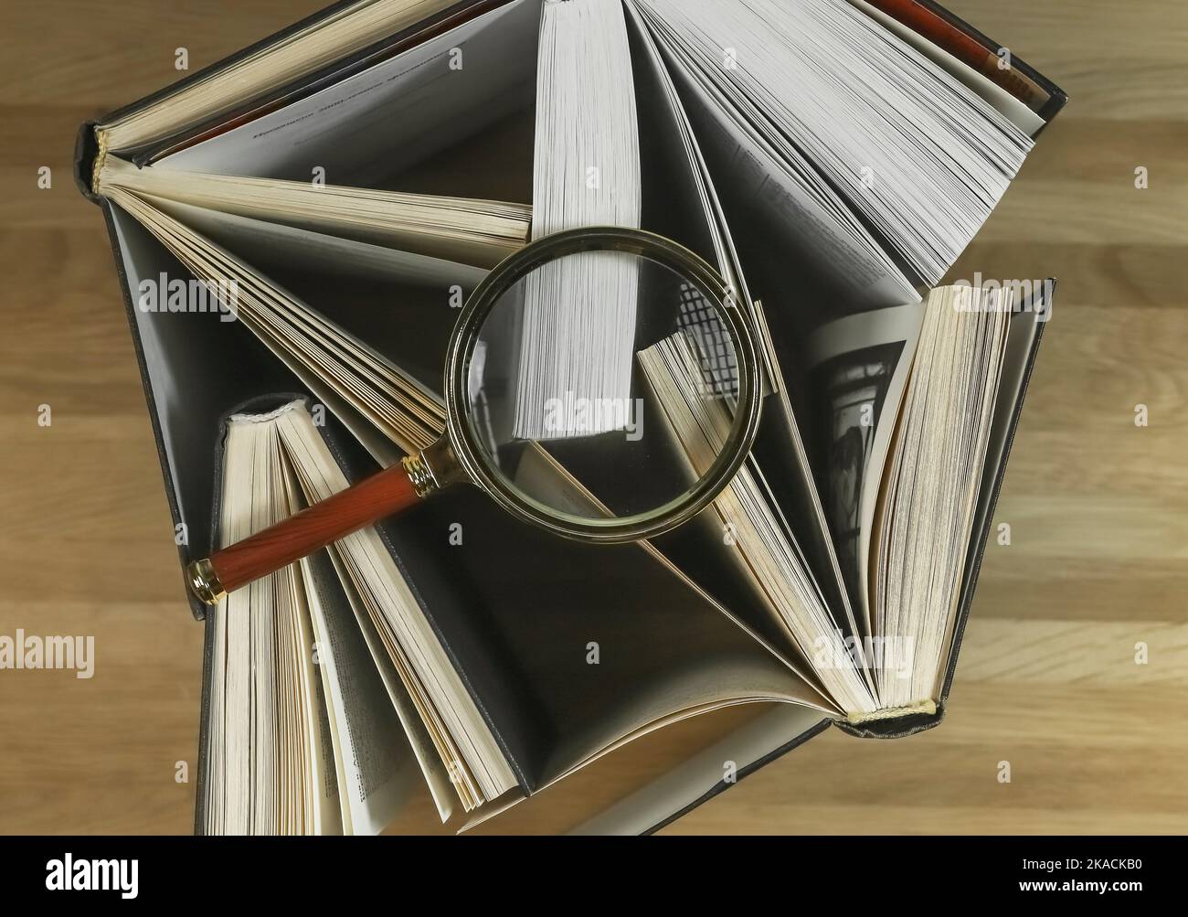 Magnifying glass over books on wood table, top view. Reading and ...