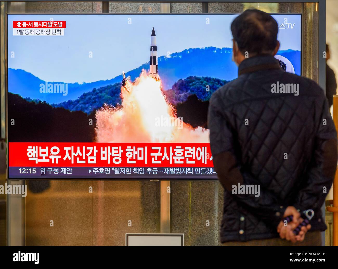 A man watches a television screen showing a news broadcast with file ...