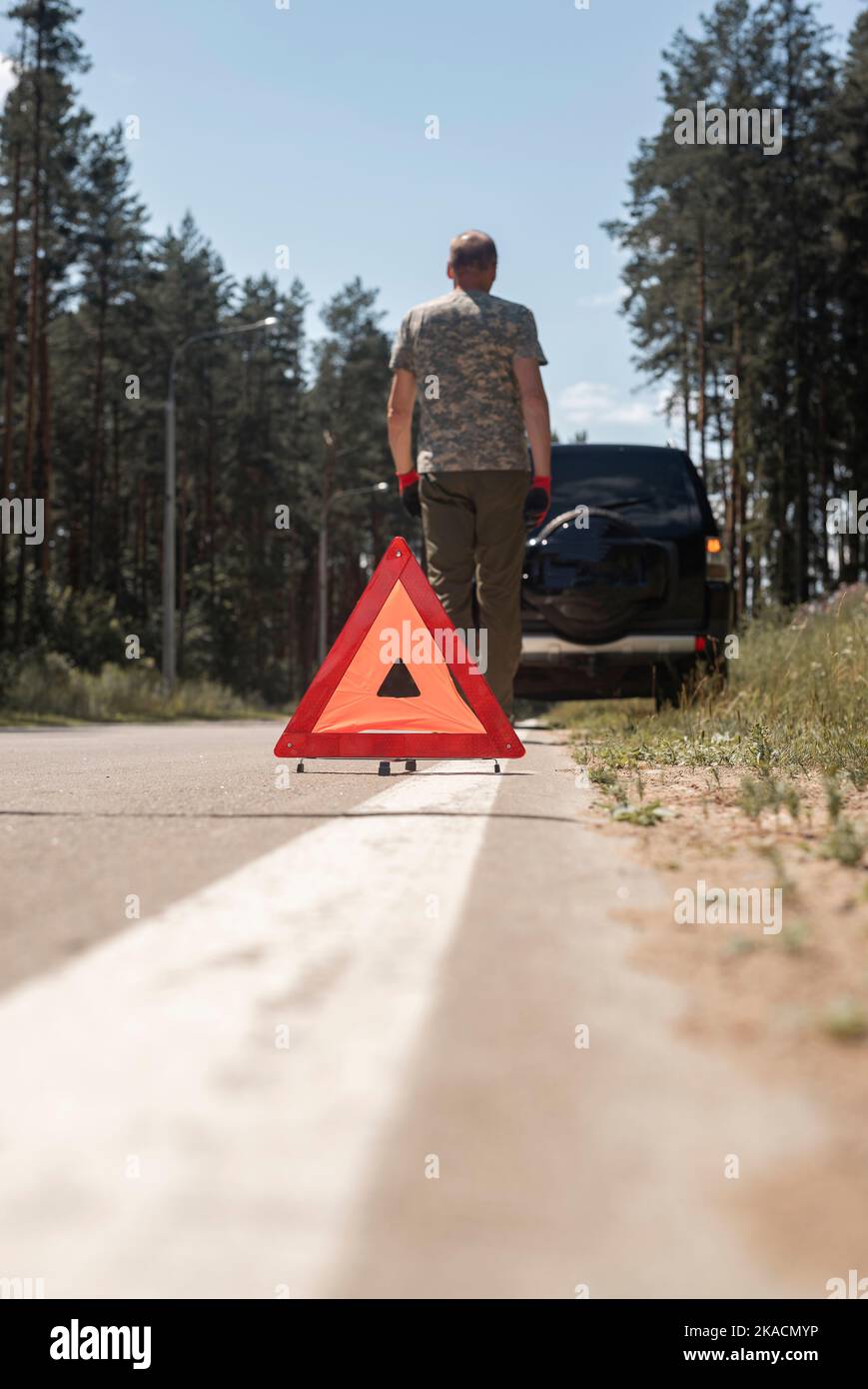 Triangle caution sign on road side on white line near broken car with ...