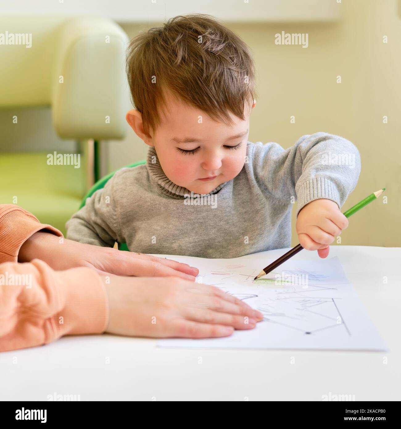 Mother teaches to draw toddler baby with a pencil on a white sheet of ...