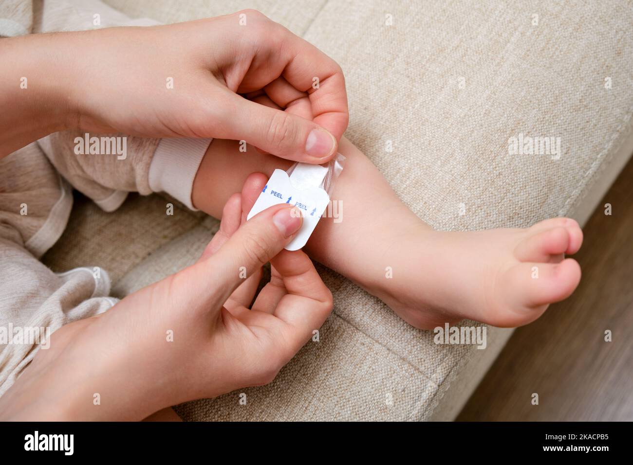 Mother woman sticks a medical adhesive plaster on the toddler baby leg ...