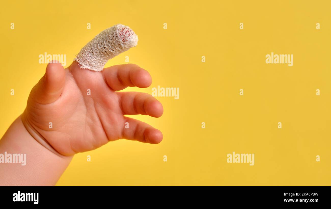 Baby s hand with a bandaged finger on a yellow studio background, copy ...