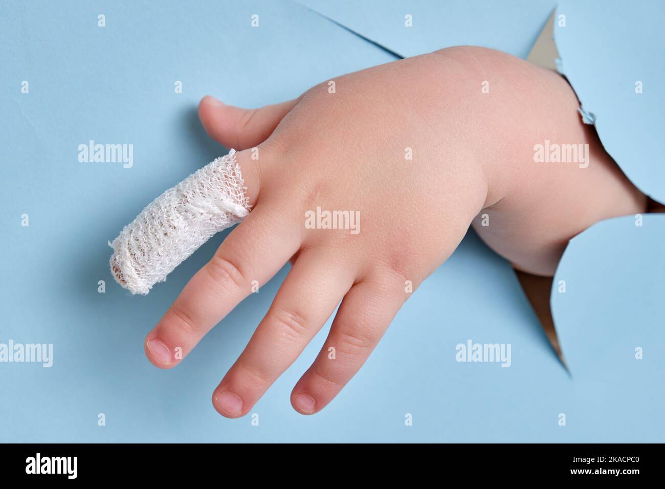 Baby s hand with a bandaged finger on a blue studio background, close ...
