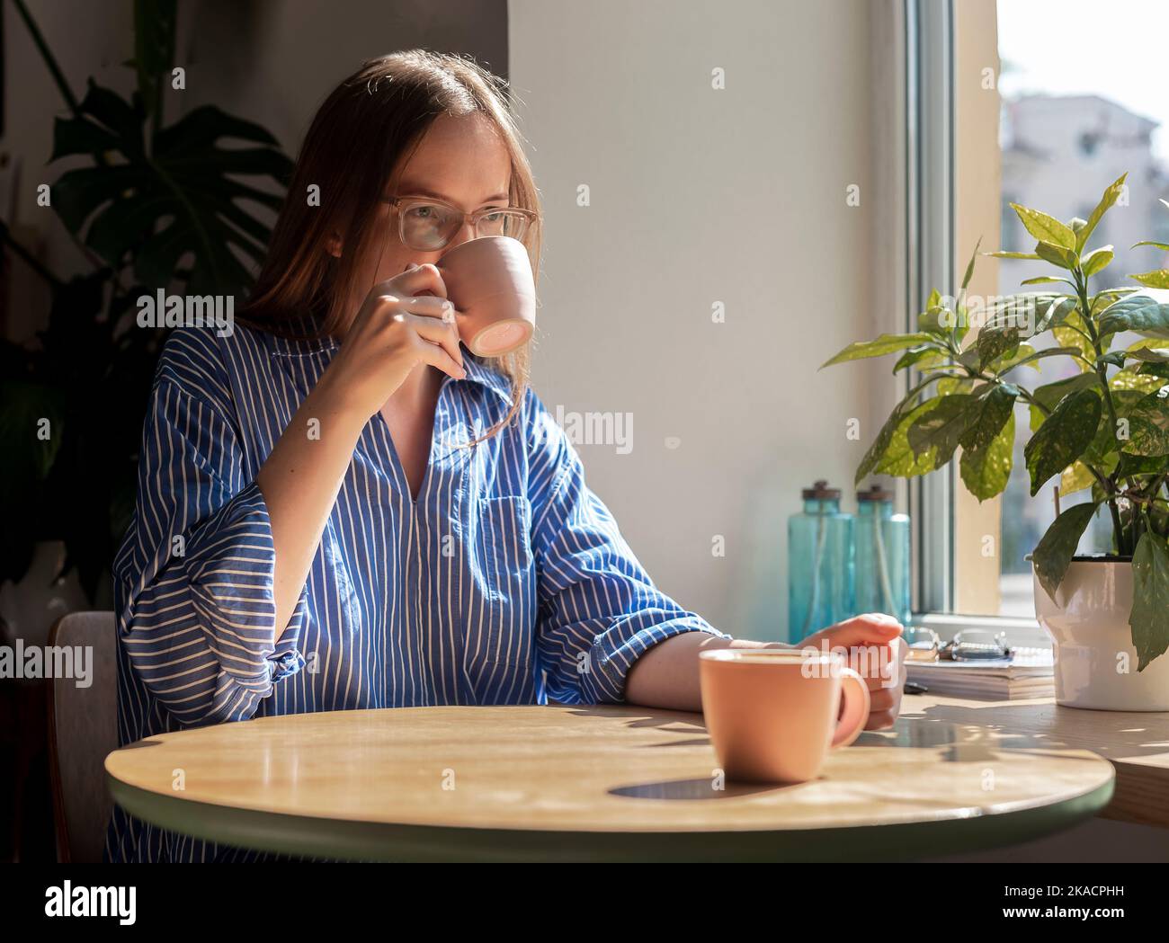 Young woman in glasses sitting by wood table in coffee shop and ...