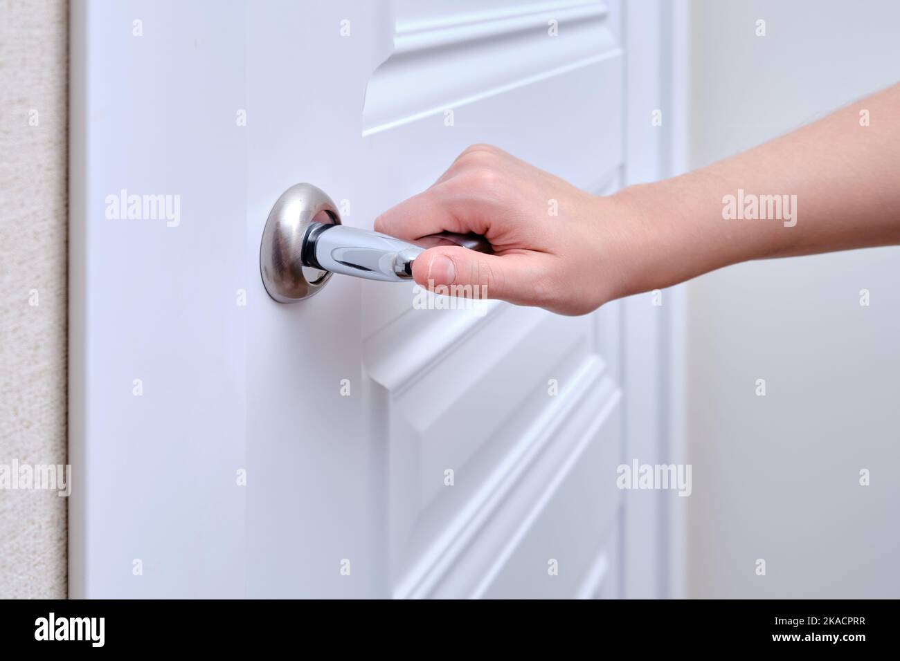 A woman opens the door holding the handle, hand close-up. White wooden ...