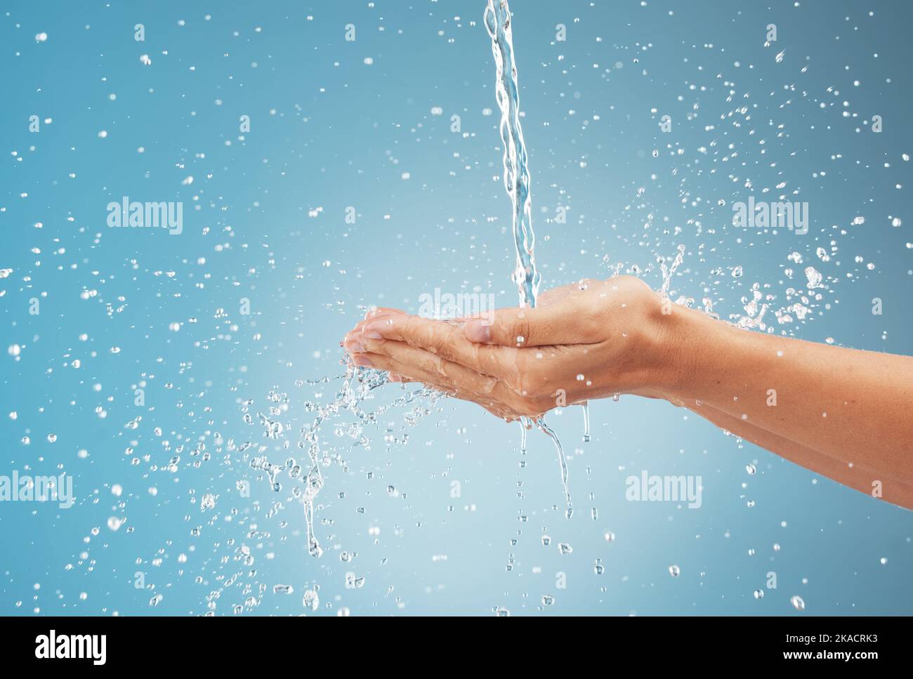 Woman, hands and water splash on blue background in studio for ...