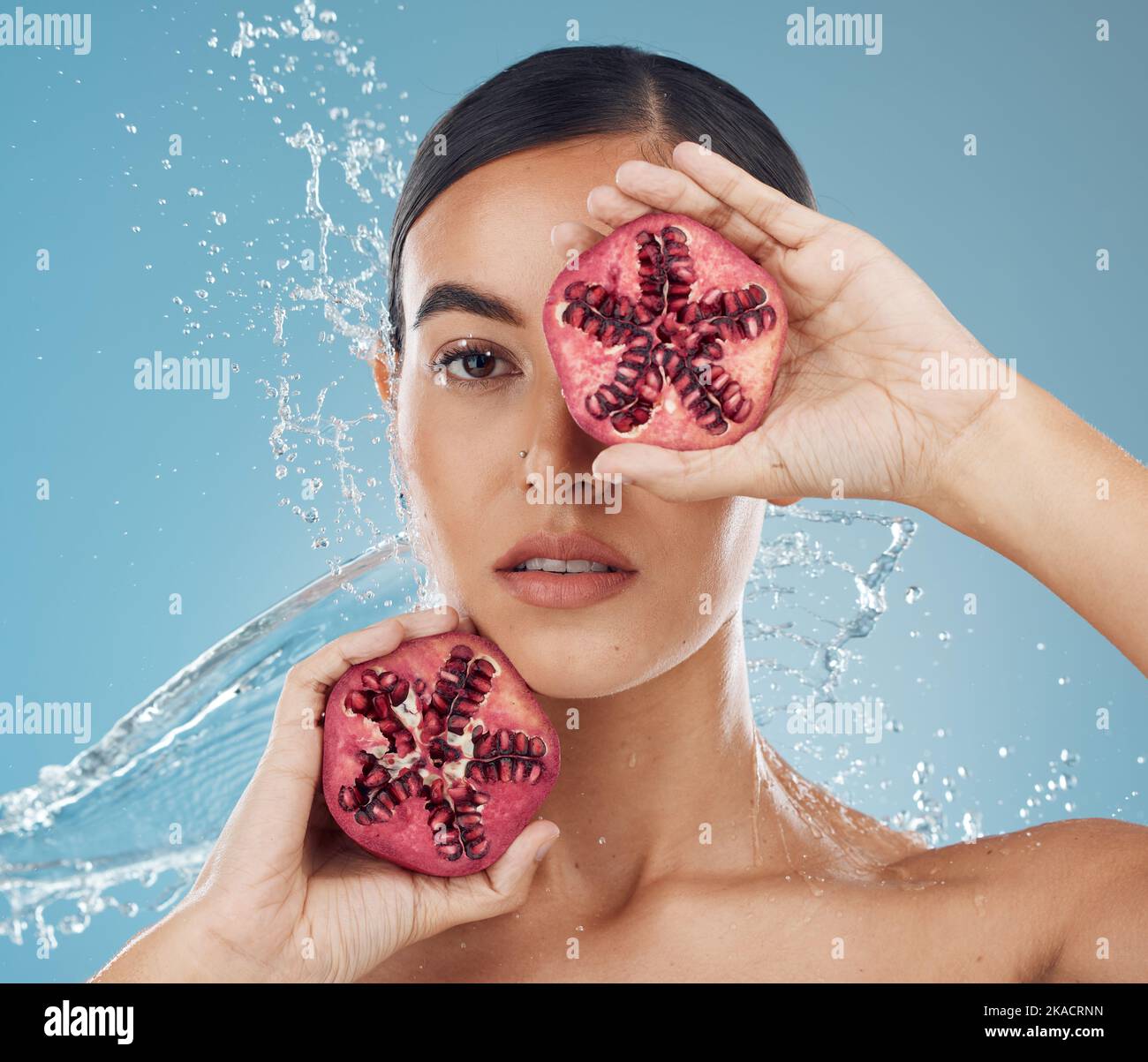 Pomegranate, skincare and beauty woman with water splash in studio blue ...