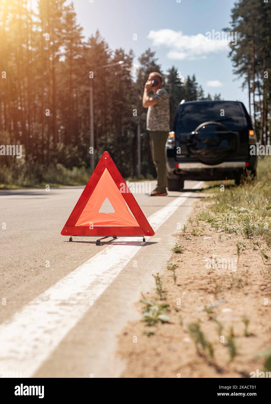 Triangle caution sign on road and man speaking on mobile phone, waiting ...