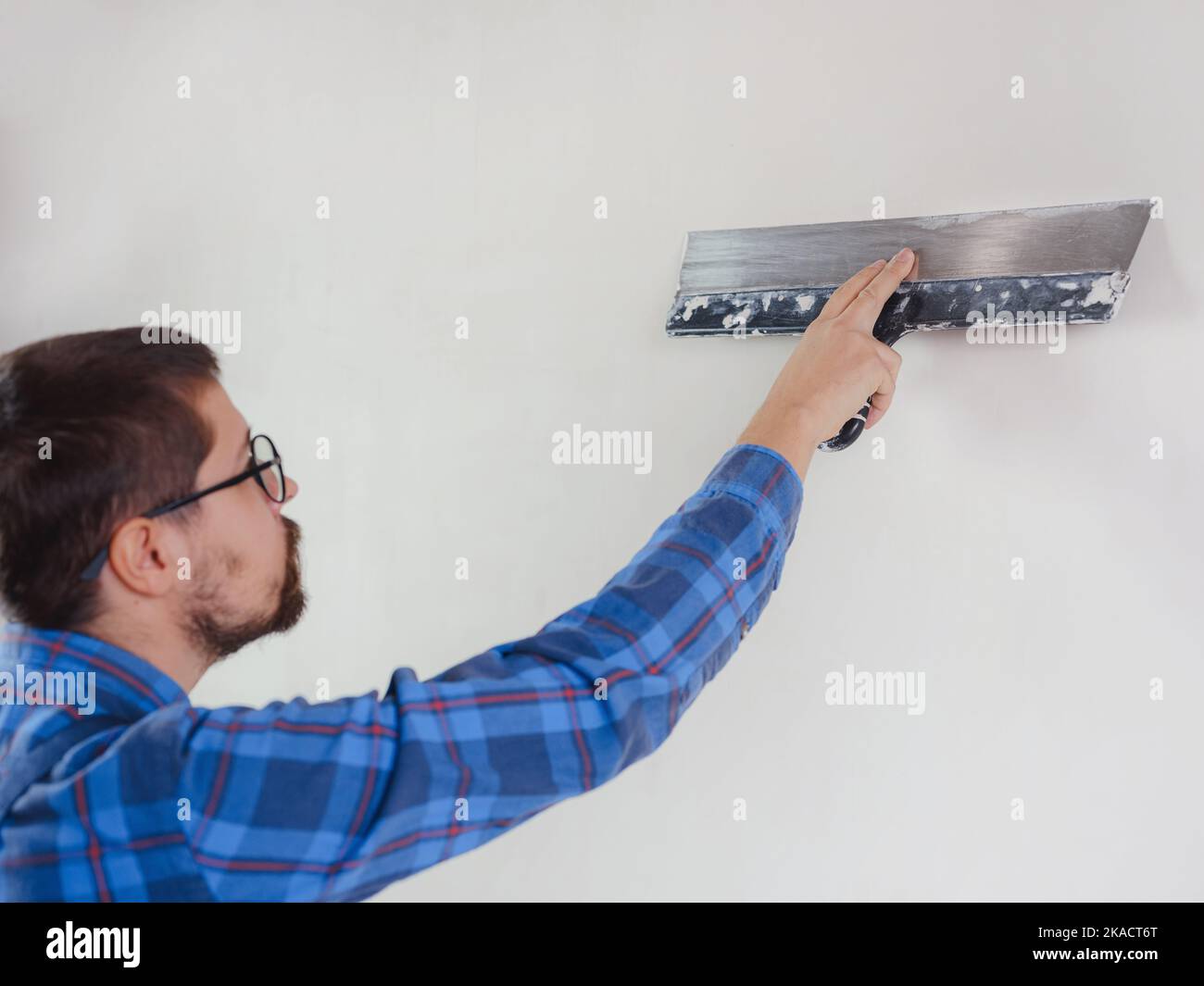 Young adult man hand using spatula and plastering white wall with fresh ...