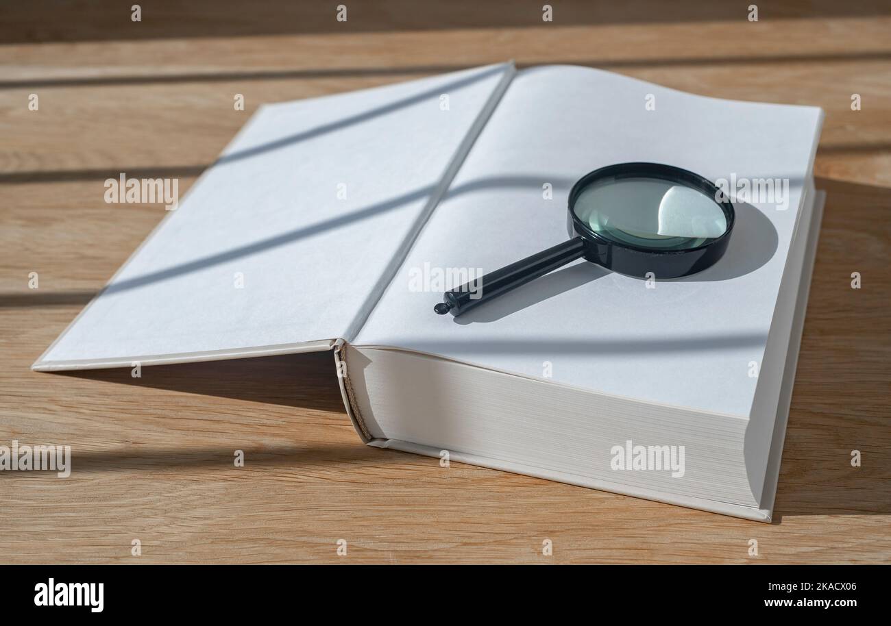 Magnifying lens with open thick book on wood desk with day light. Start ...