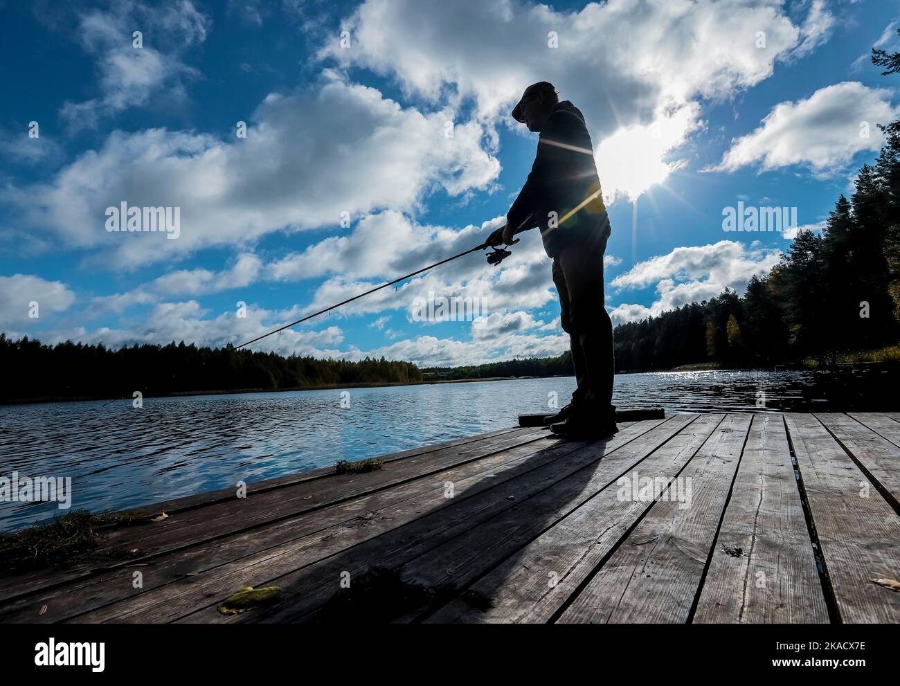 Fisherman silhouette standing on wood pier catching fishes on reel rod ...