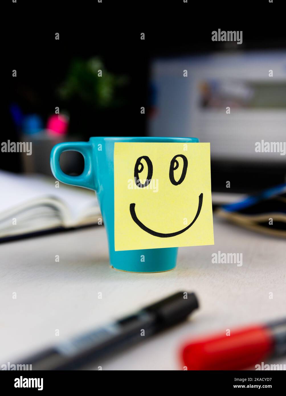 Smiling face drawn on sticky note on a cup of coffee at the office desk ...
