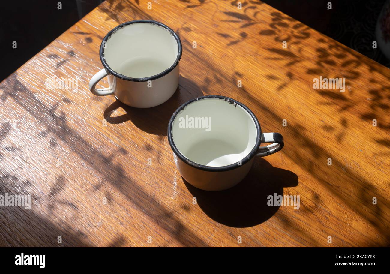 Two metal white cups with water on old wooden table with sin light and ...
