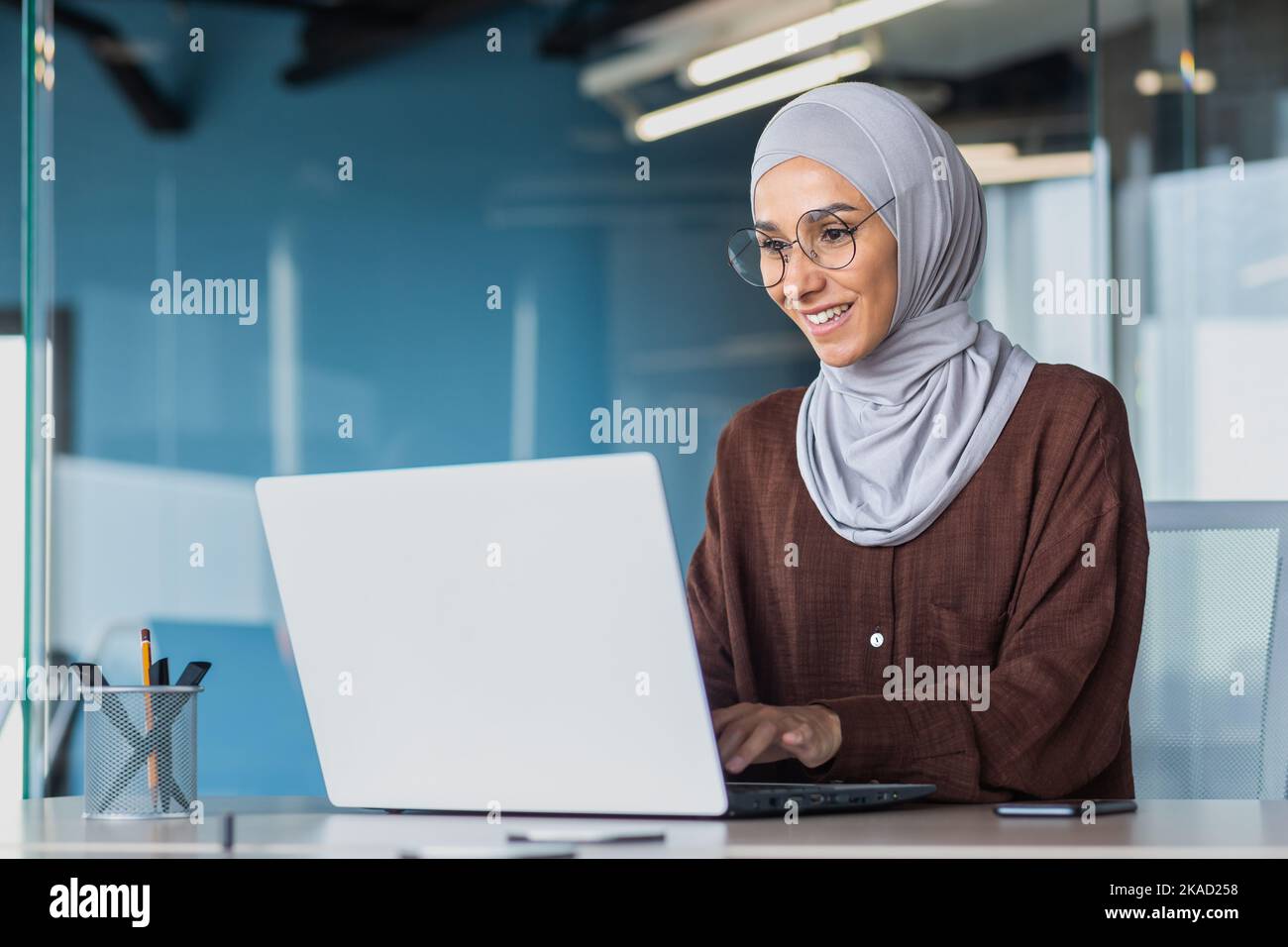 Happy and successful business woman in hijab working with laptop inside ...