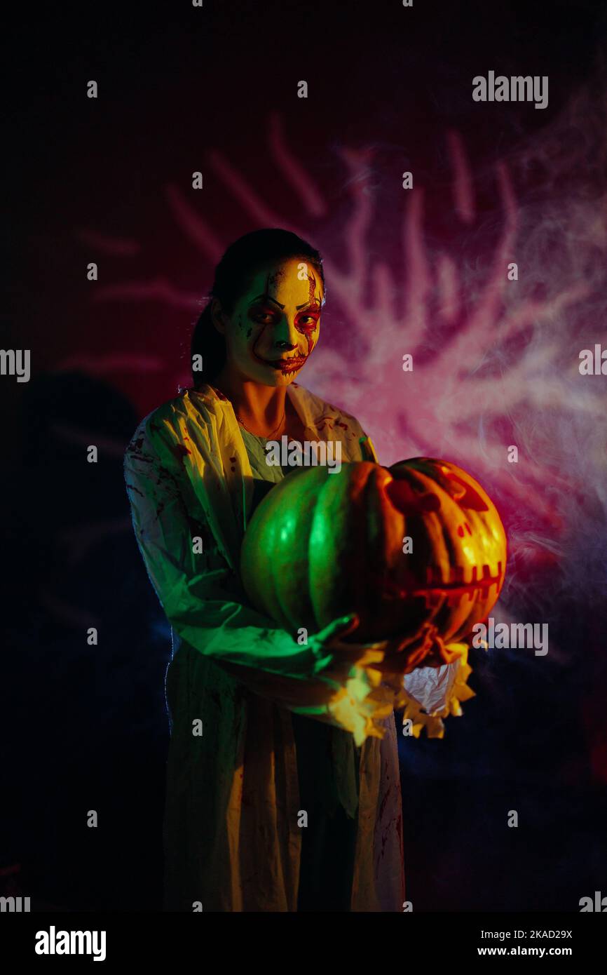 Young woman holds pumpkin in her hands and portrays bloodthirsty zombie ...