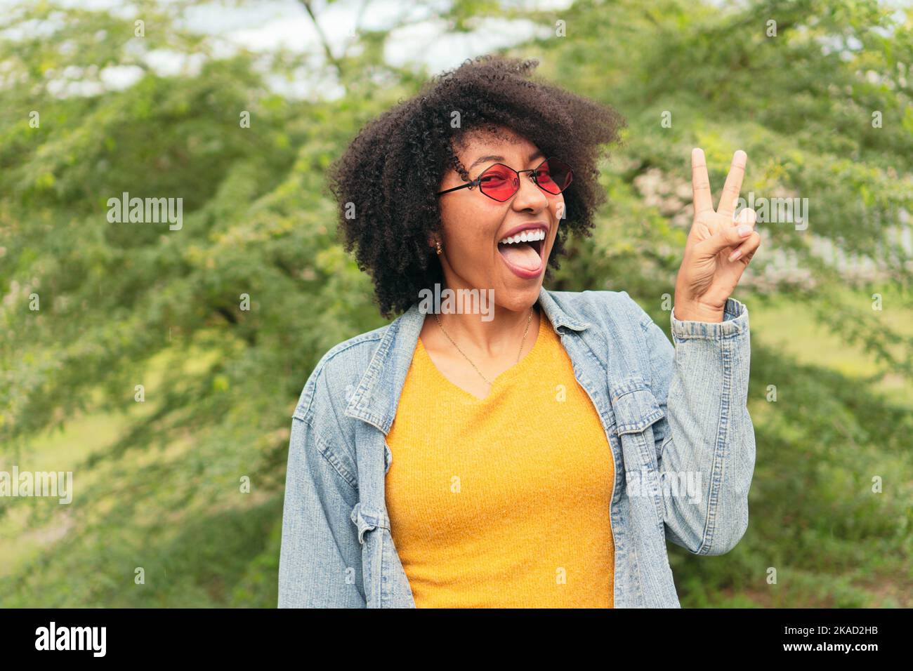 Afro woman making peace sign with fingers while posing over a natural ...