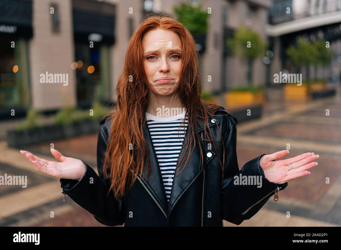 Portrait of distraught young woman with long red-hair standing with wet ...