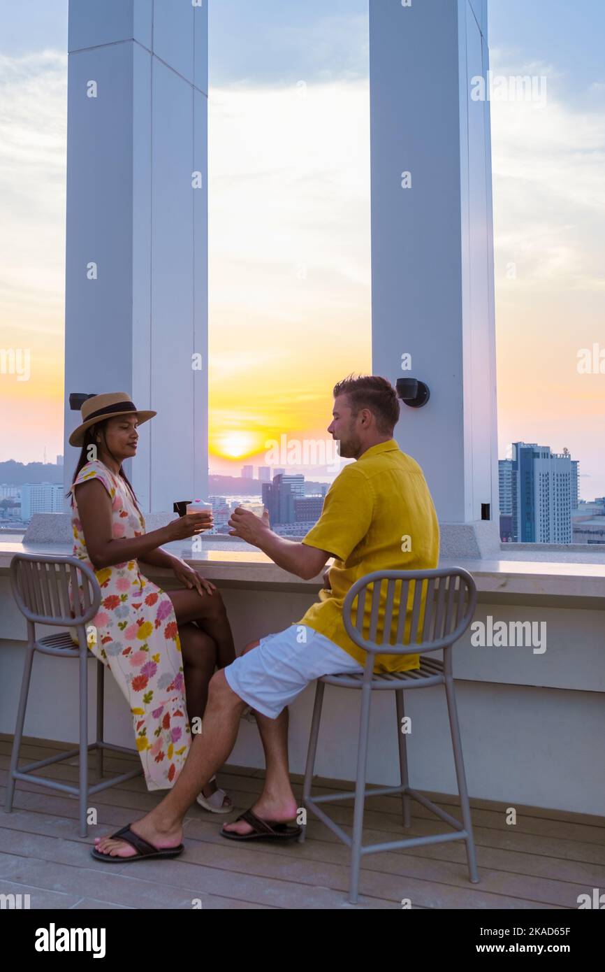 Thai women and European men watching sunset on a rooftop bar, couple of ...