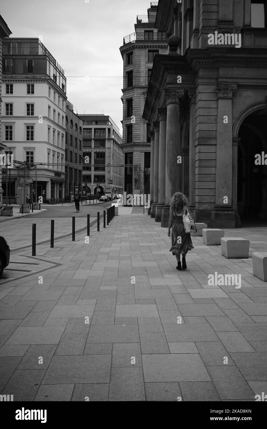 A grayscale of a female walking in a square on a sunny day Stock Photo ...
