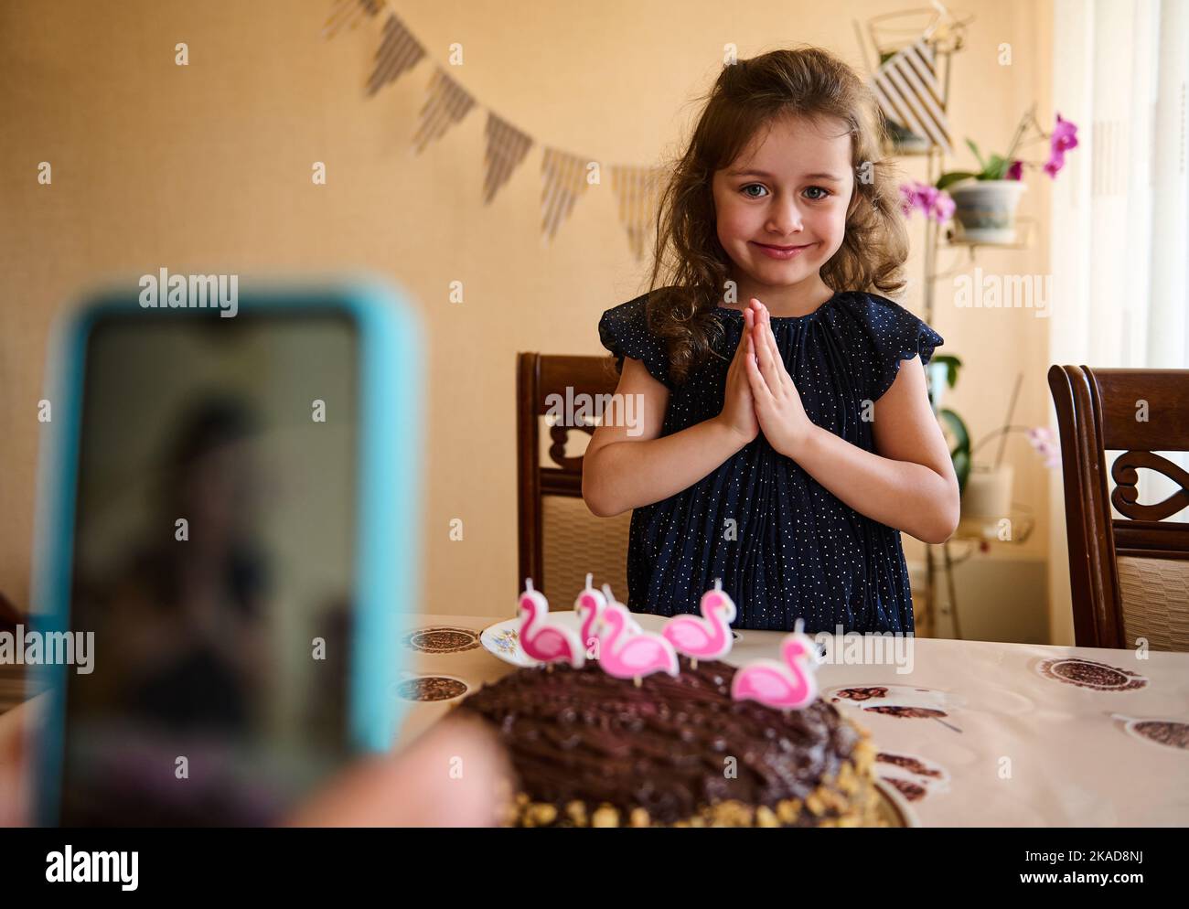 Adorable birthday girl in navy dress, holds her palms together, makes a ...