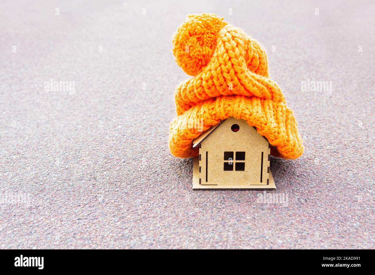 Toy wooden house with chunky warm hat on top isolated on gray. Energy ...