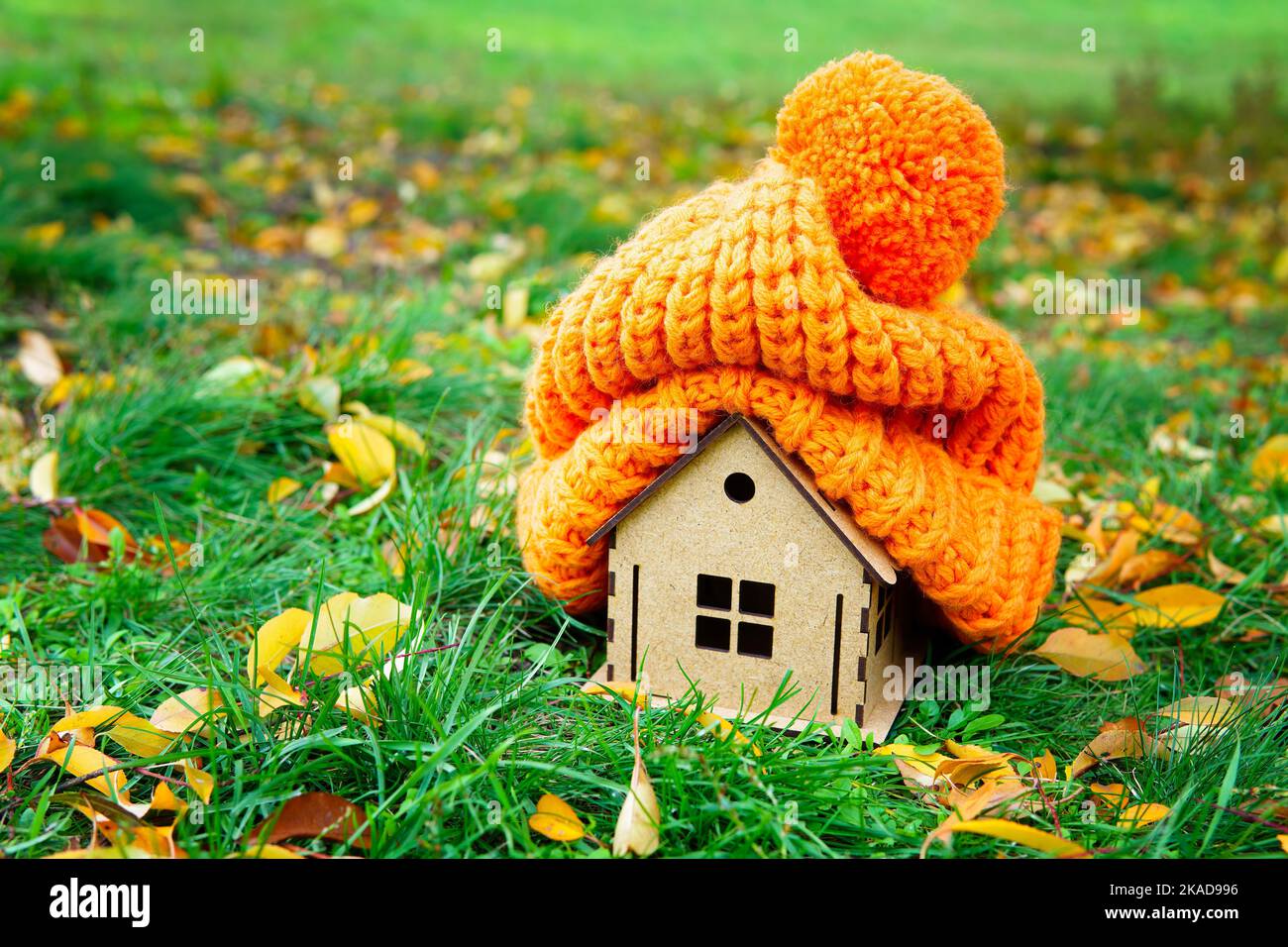 Chunky knitted hat put on a wooden house figurine placed on a green ...